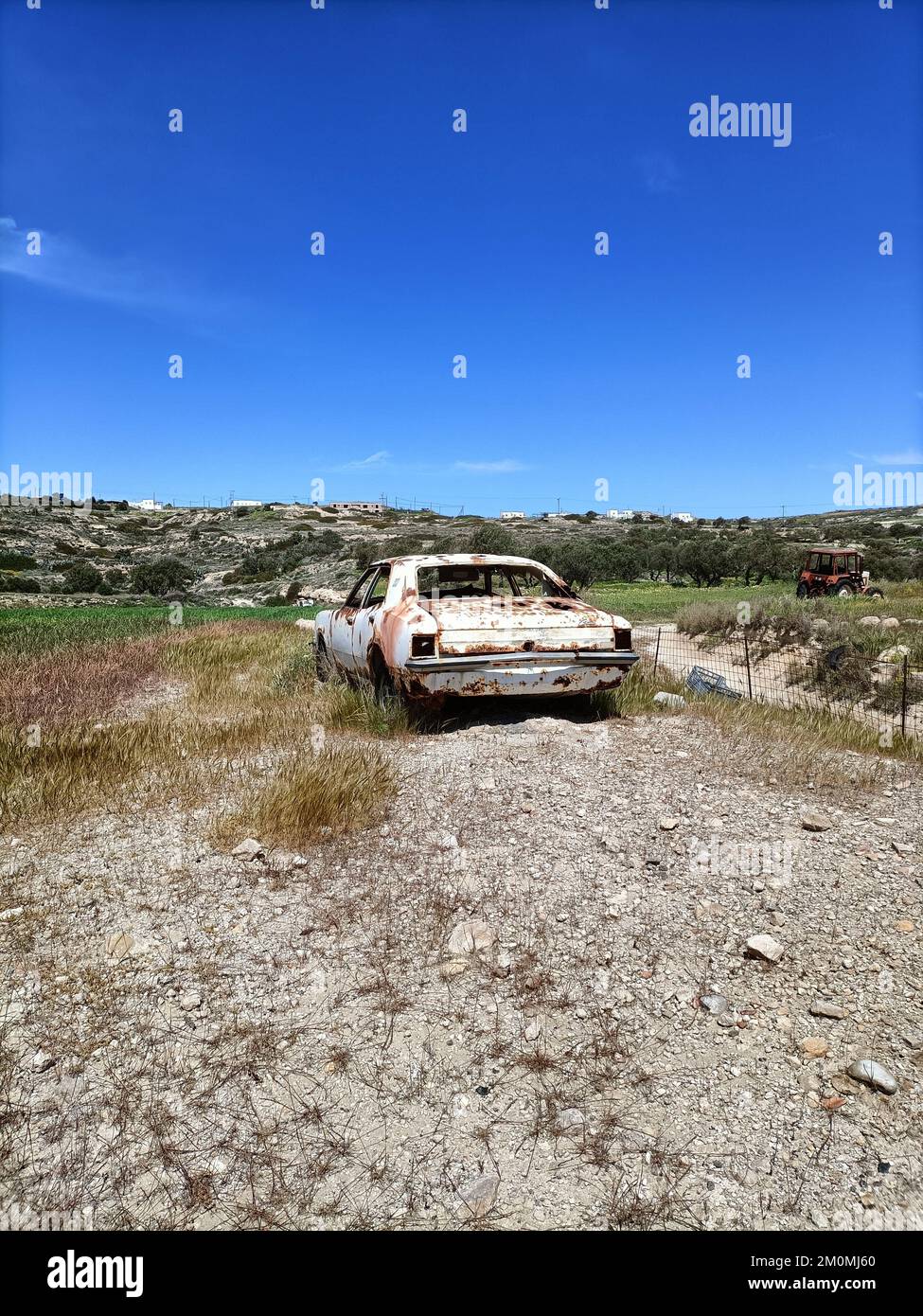 A vertical shot of an old rusty white car abandoned in the middle of a ...