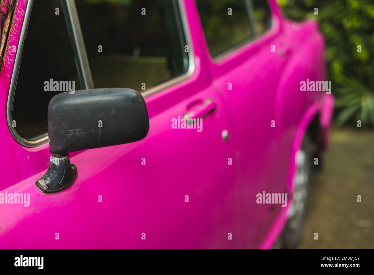 A selective focus shot on the side mirror of a pink retro car standing ...