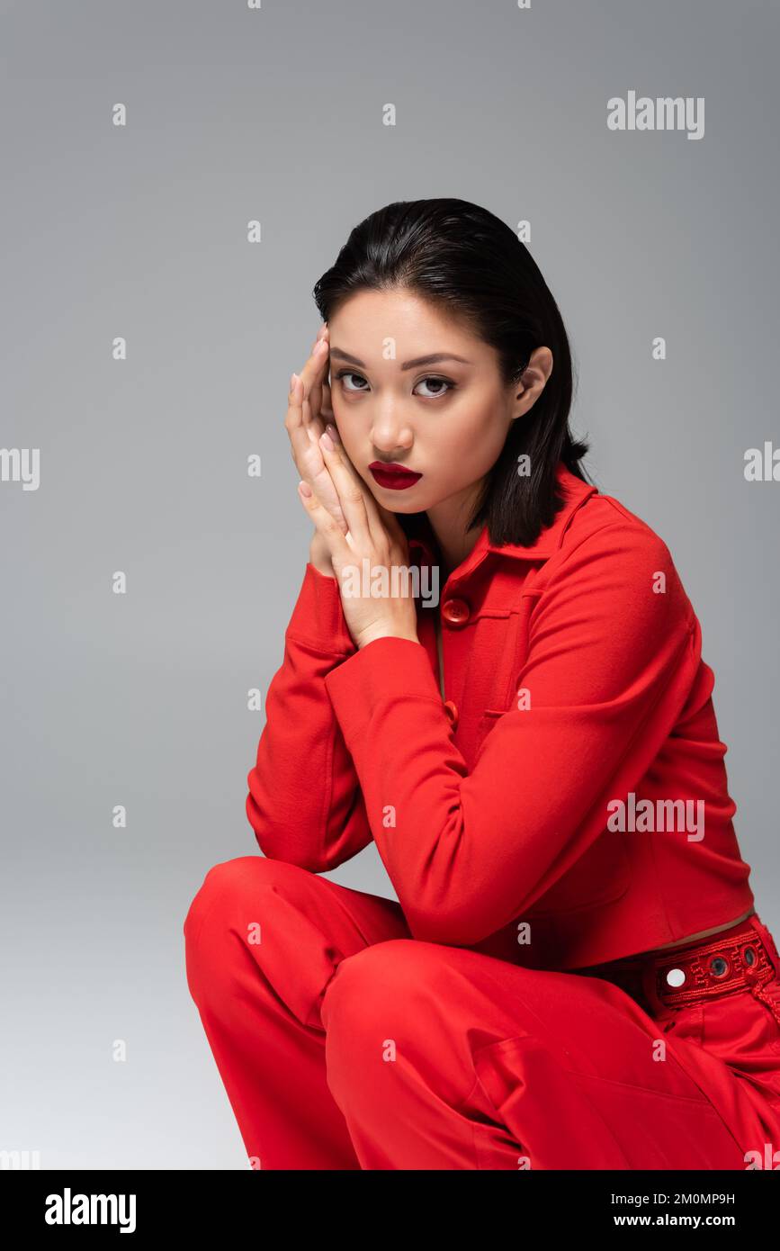 stylish asian woman in red elegant attire sitting on haunches with ...