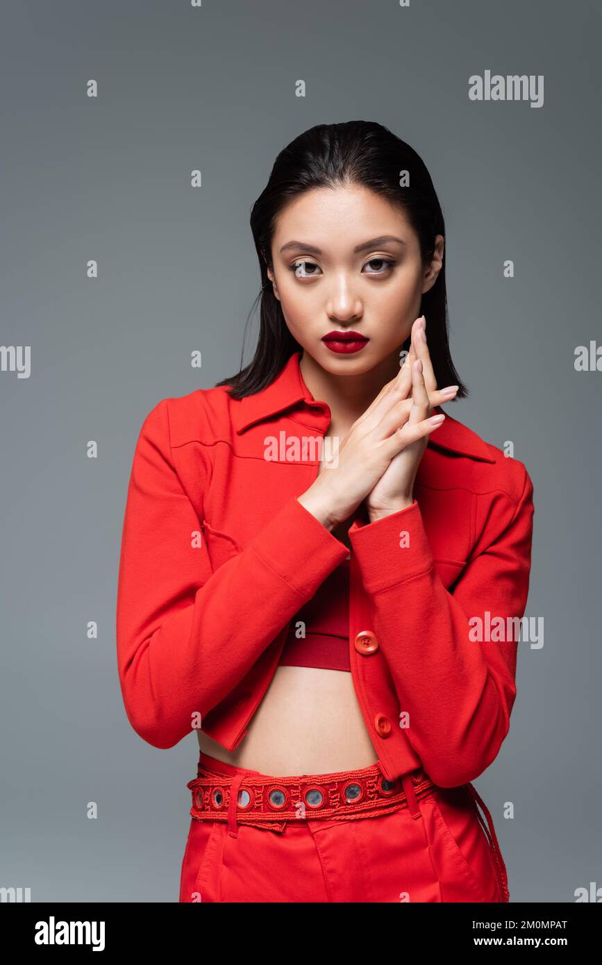 brunette asian model in red fashionable jacket looking at camera ...
