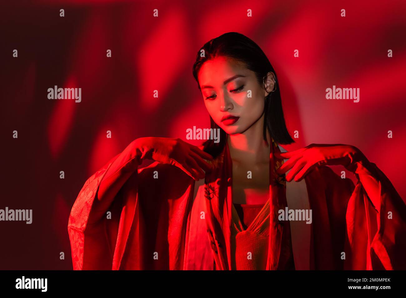 elegant asian woman in gloves and kimono cape posing on red background ...