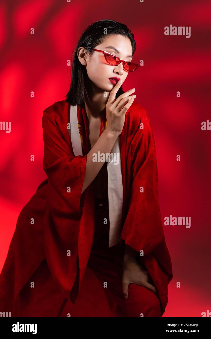 brunette asian woman in kimono cape and sunglasses showing hush sign on ...