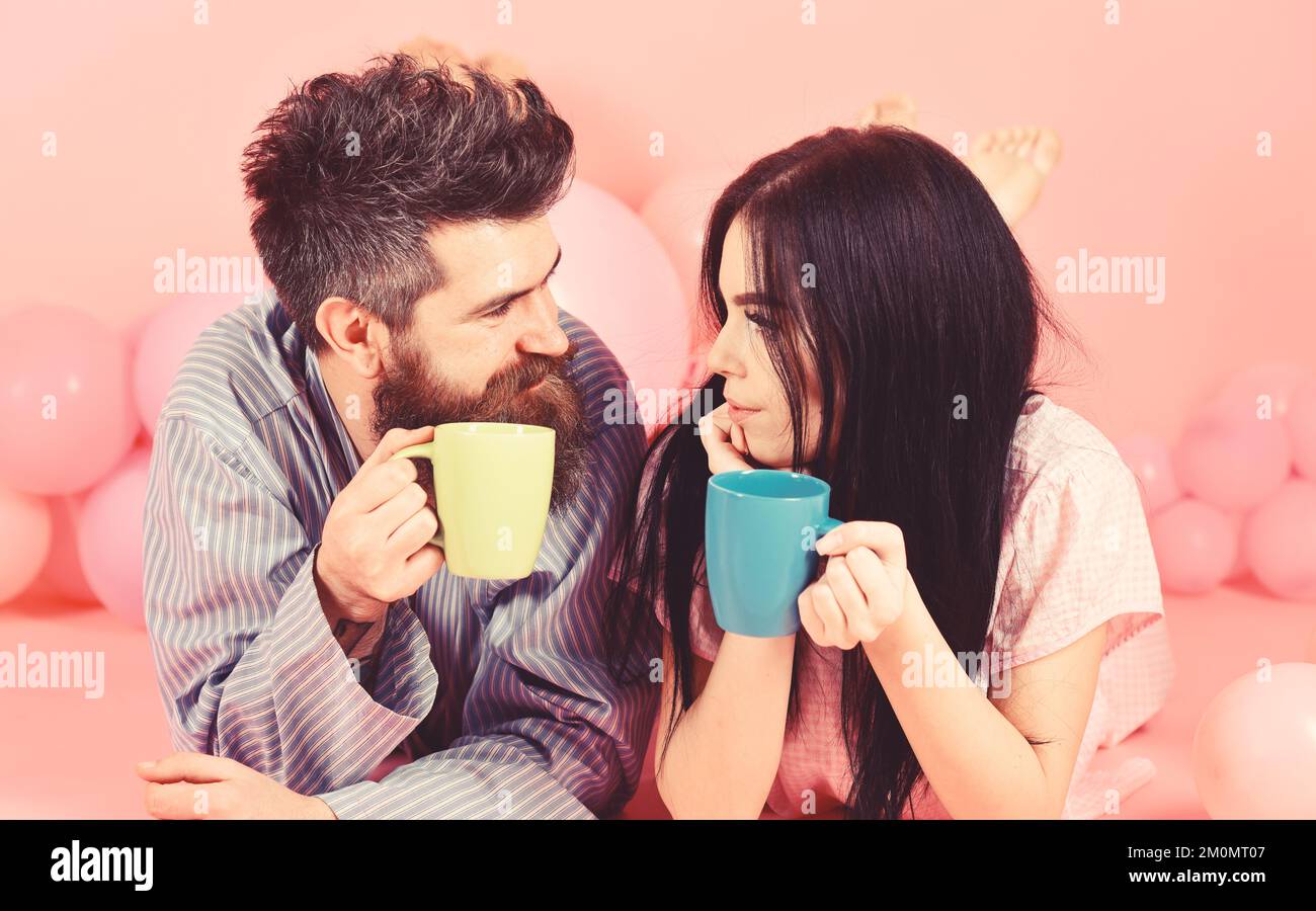 Young couple drinking coffee in bed, pink background. Couple relax in ...