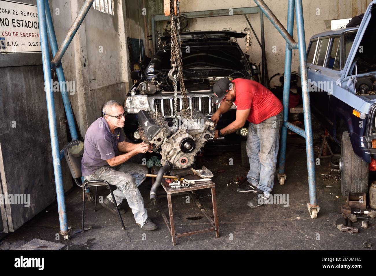 A father and son work together in their garage repairing a V8 engine ...