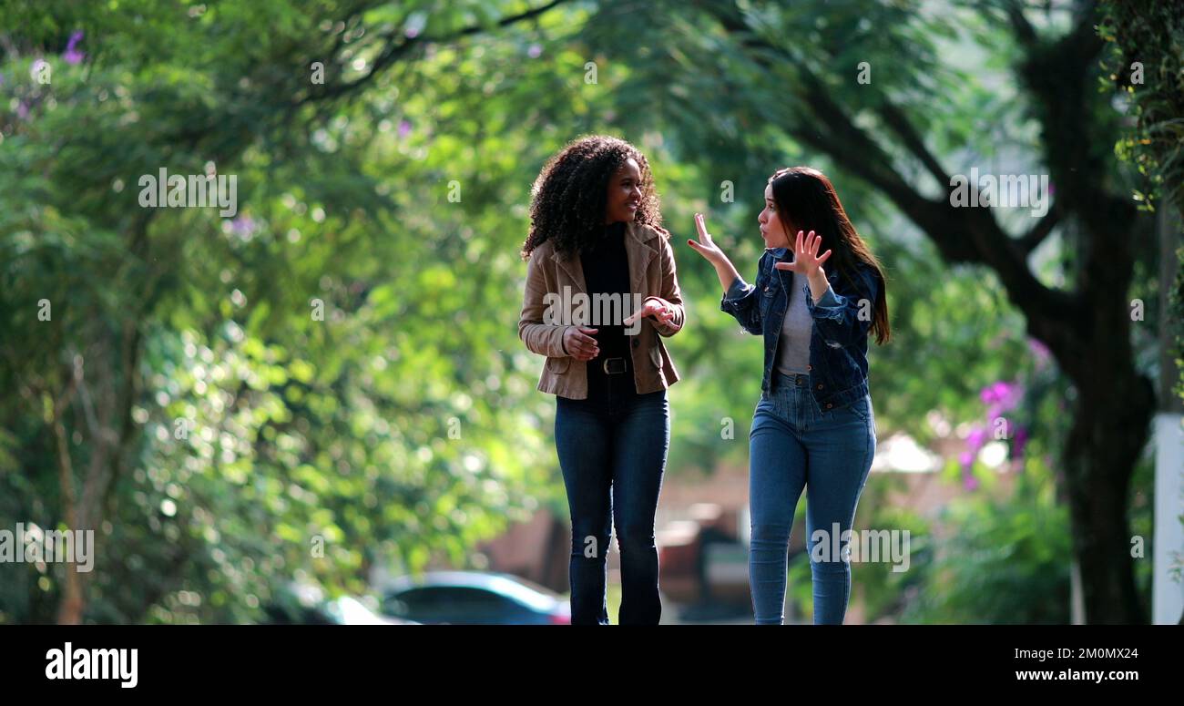 Two diverse young women laughing together while walking outside in ...