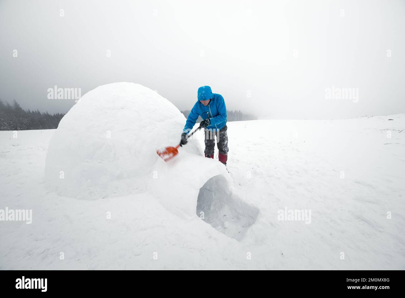 Man in blue jacket building igloo in the high mountain. Fantastic ...