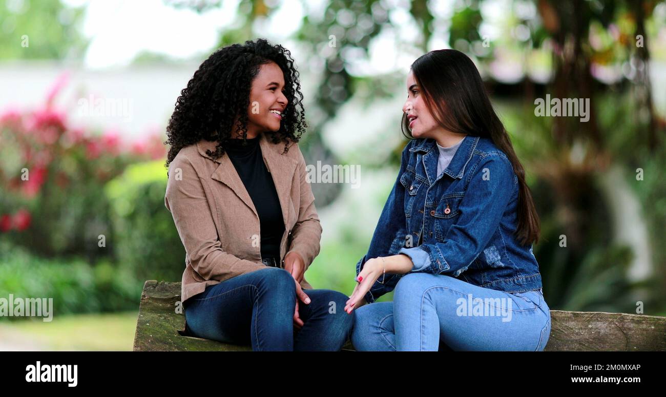 Two diverse girls talking outside together, real life laugh. Female friends bonding chatting ...