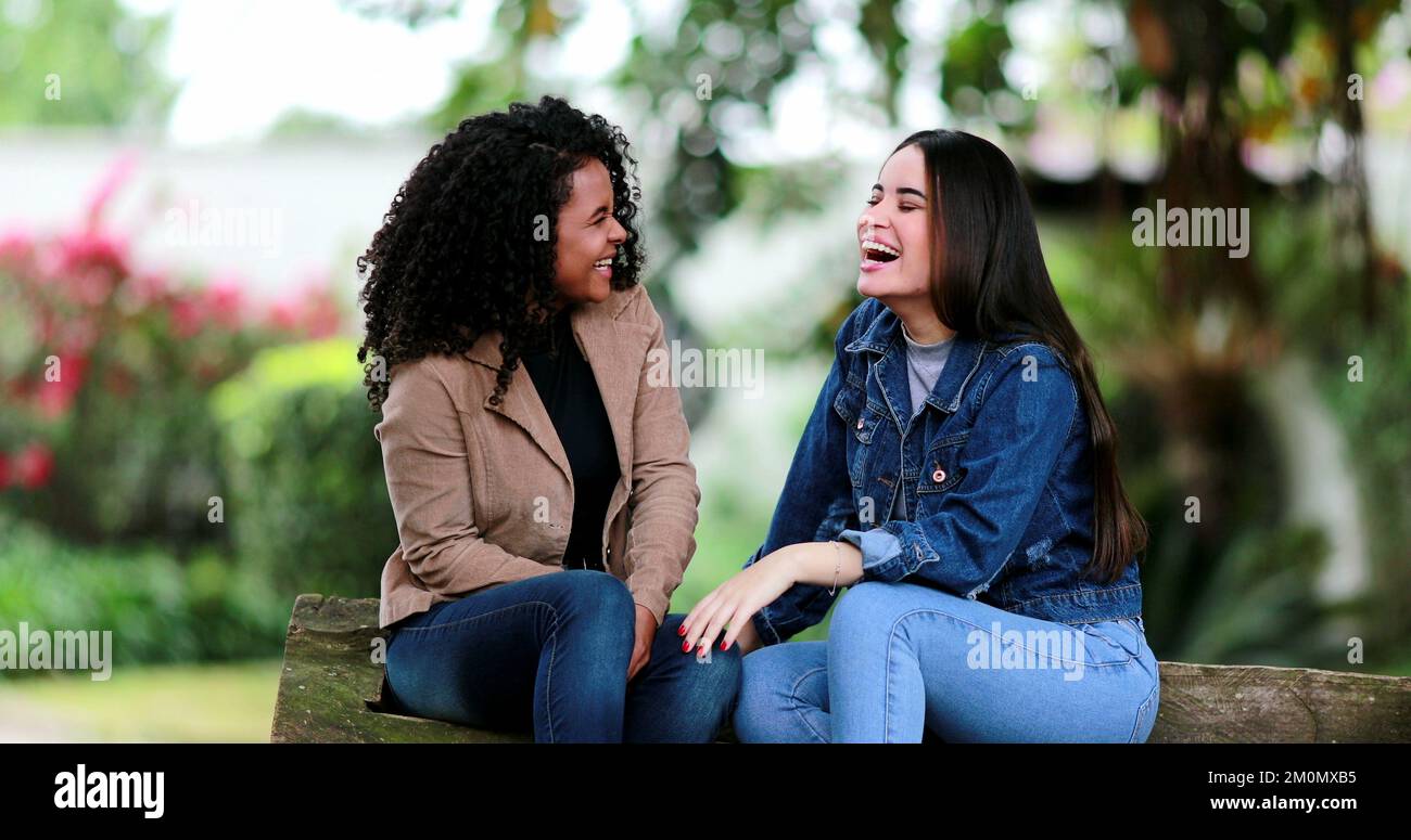 Two diverse girls talking outside together, real life laugh. Female friends bonding chatting ...