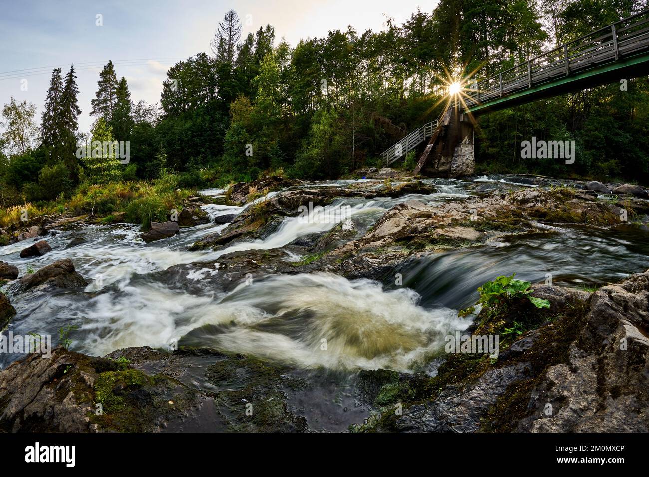 A scenic shot of a footbridge across a rocky river with silky effect ...