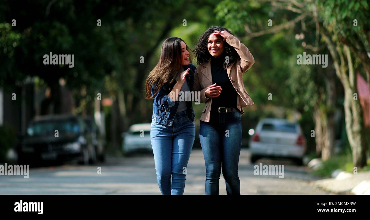 Two beautiful diverse girlfriends walking and laughing together while ...