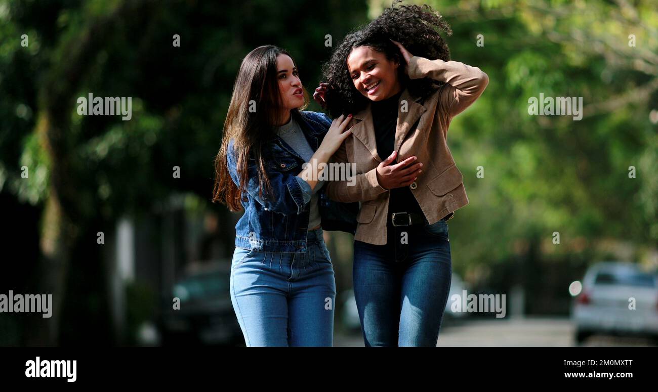 Two beautiful diverse girlfriends walking and laughing together while ...