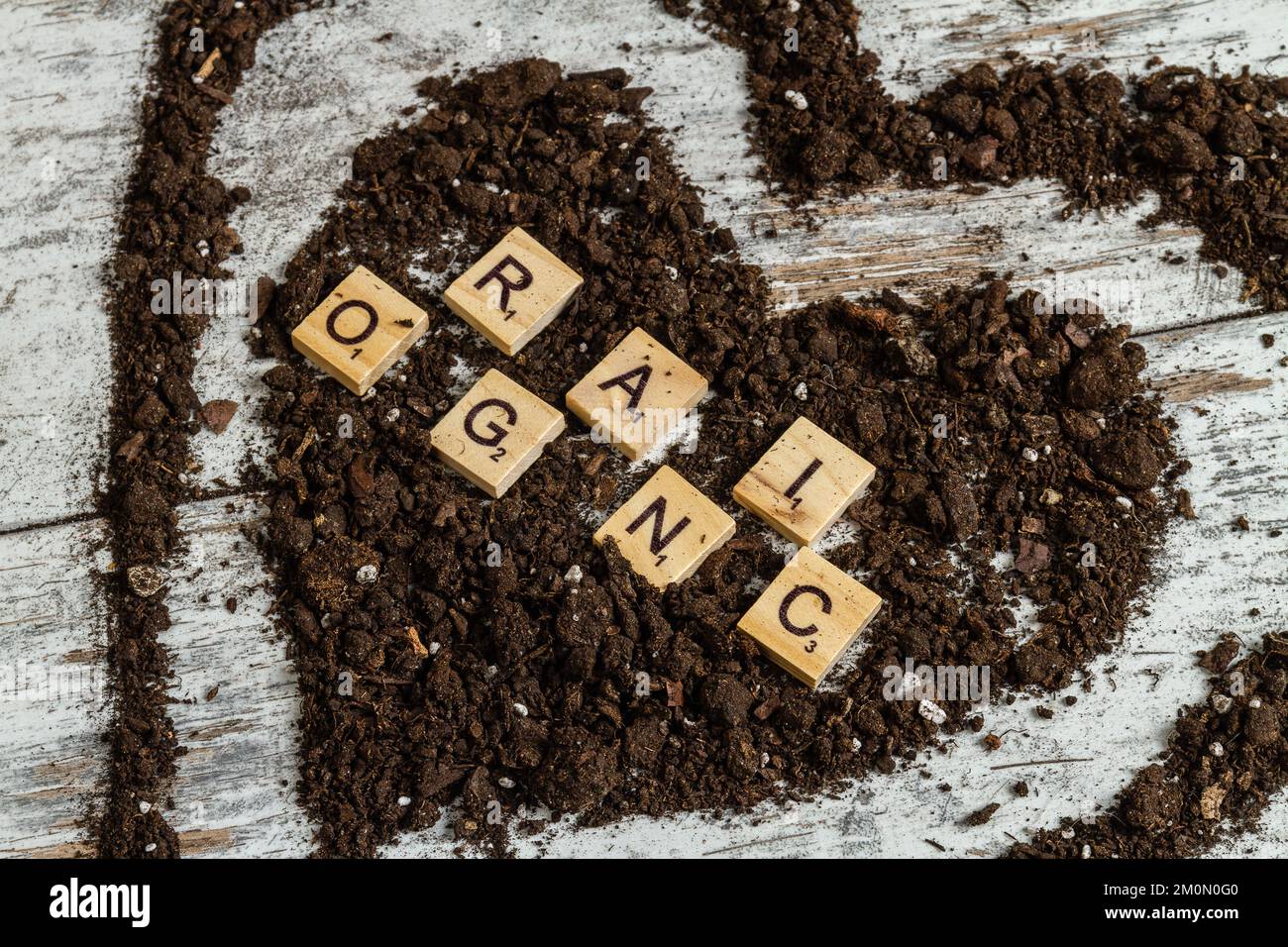 Natural black soil in a heart shape close up. Gray desk background ...