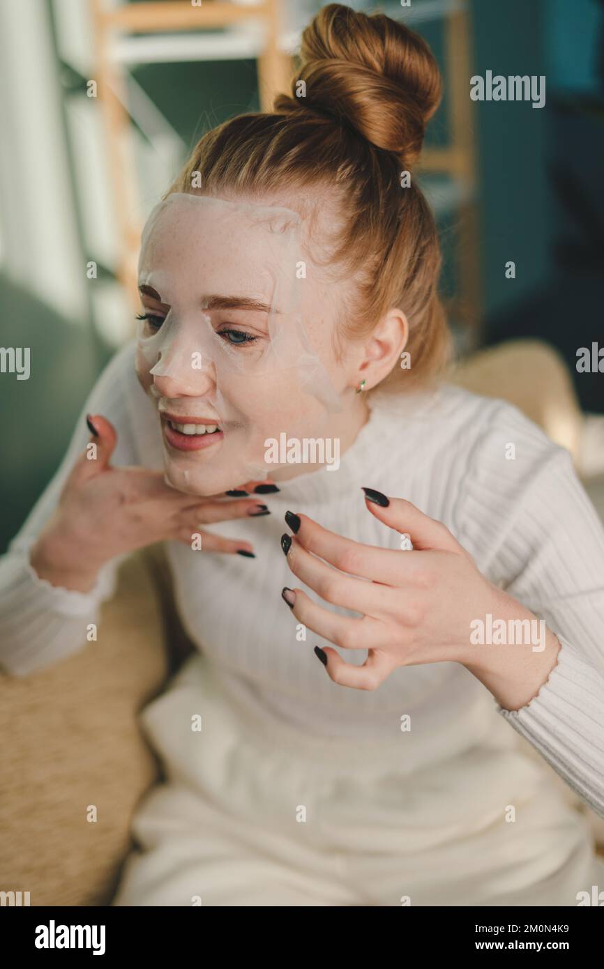 Woman applying facial paper mask at home while sitting in her living ...