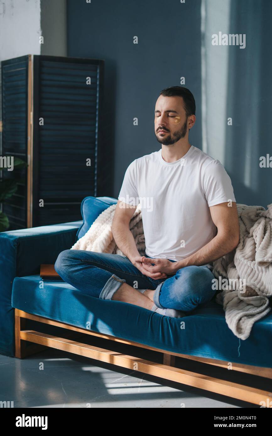 Man sitting with his legs crossed on a sofa and meditating in living ...