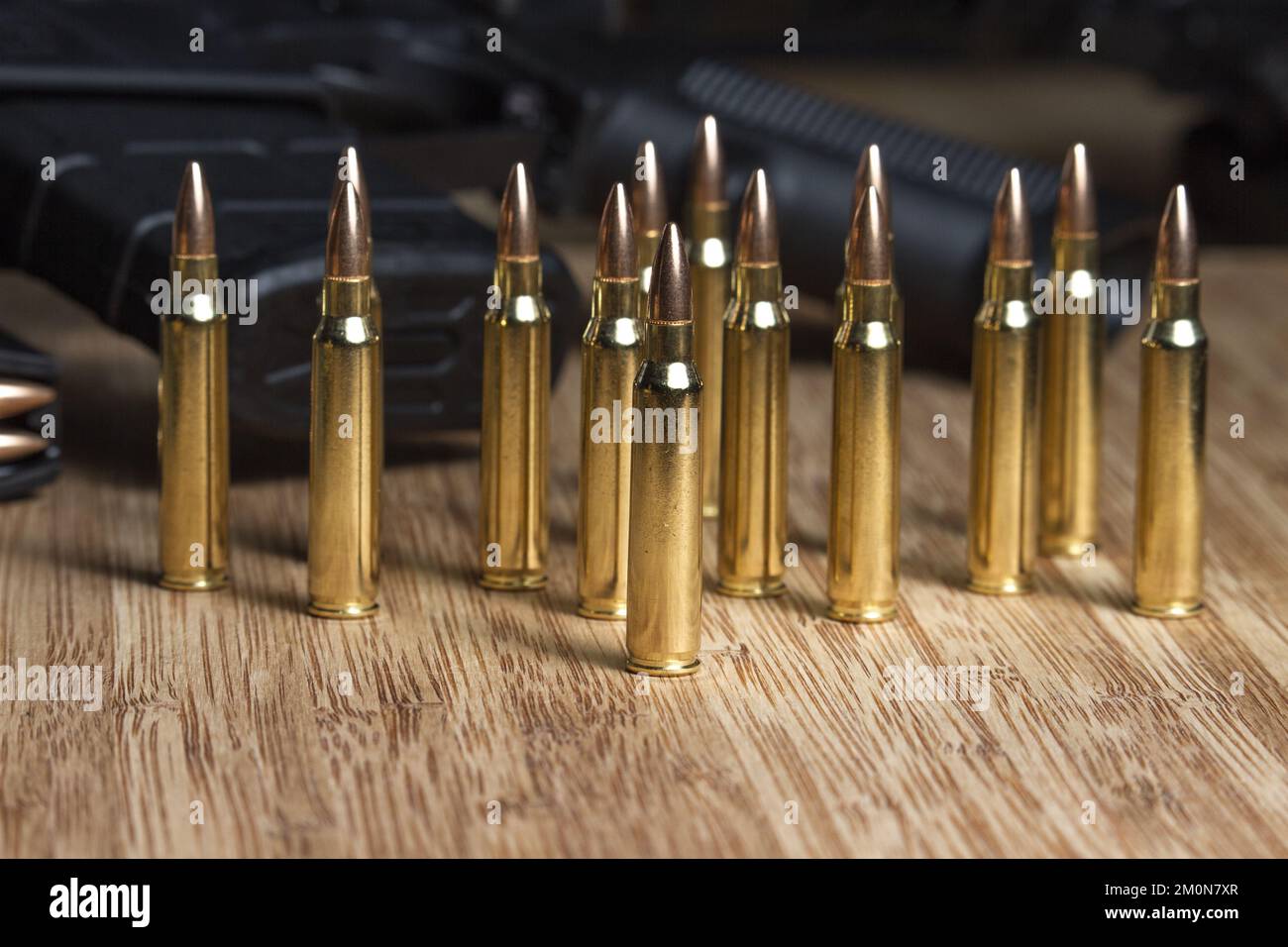Shiny 5.56mm bullets standing up on a bamboo board in front of a loaded ...