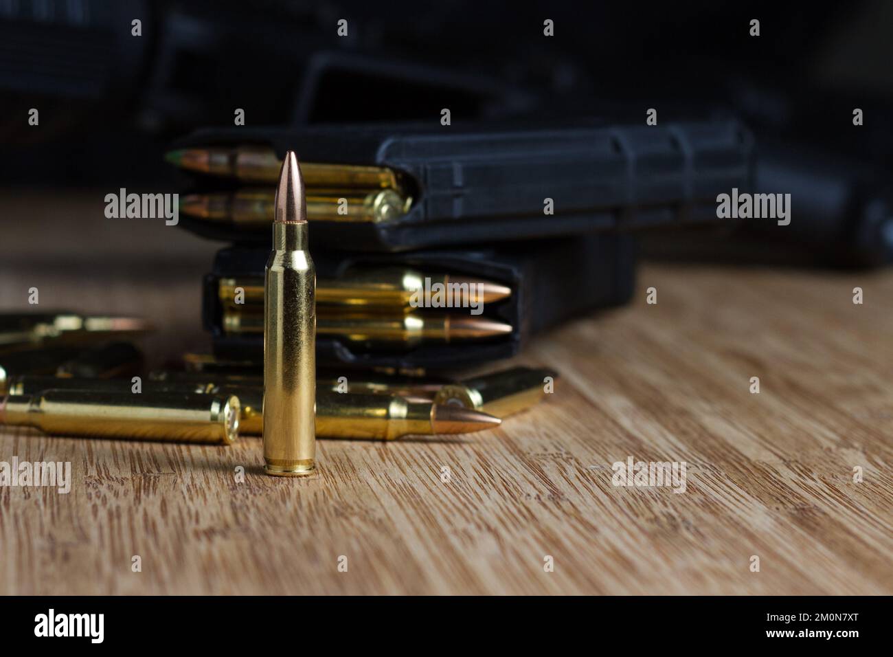 A single .223 bullet, standing in front of loose ammo and two AR-15 magazines loaded with ...