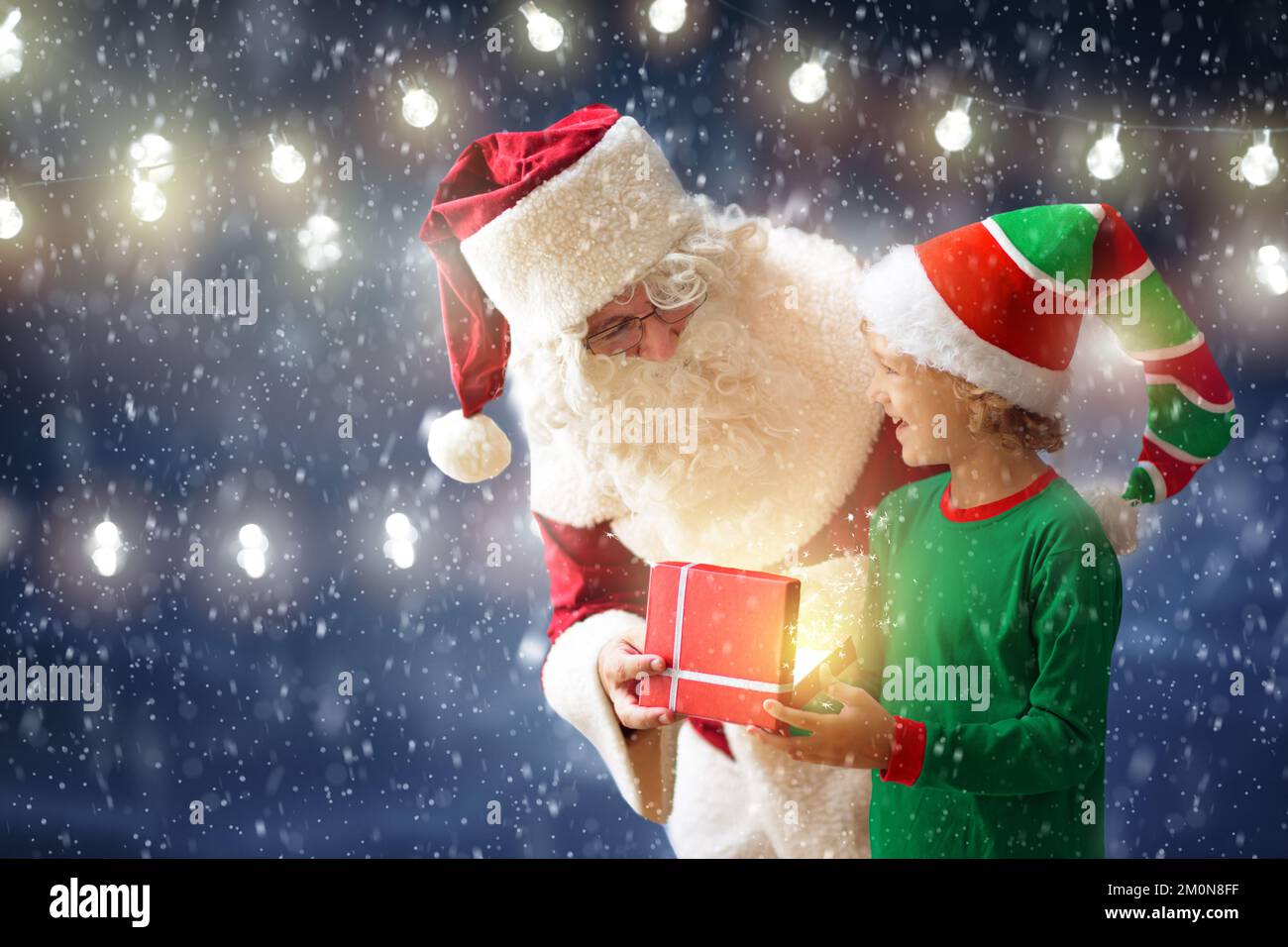 Santa and elf deliver Christmas presents. Santa Claus and little child open a gift box with ...