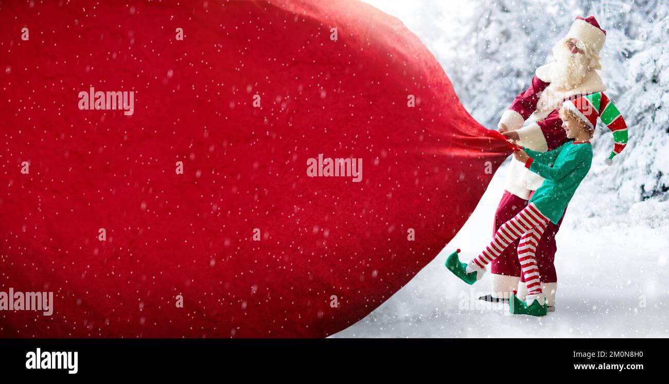 Santa and elf deliver Christmas presents. Santa Claus and little child pull a huge sack with ...
