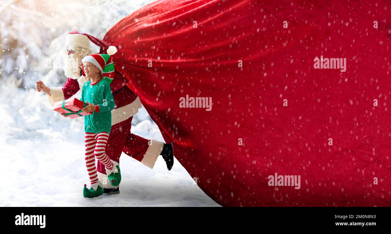 Santa and elf deliver Christmas presents. Santa Claus and little child carry a huge sack with ...