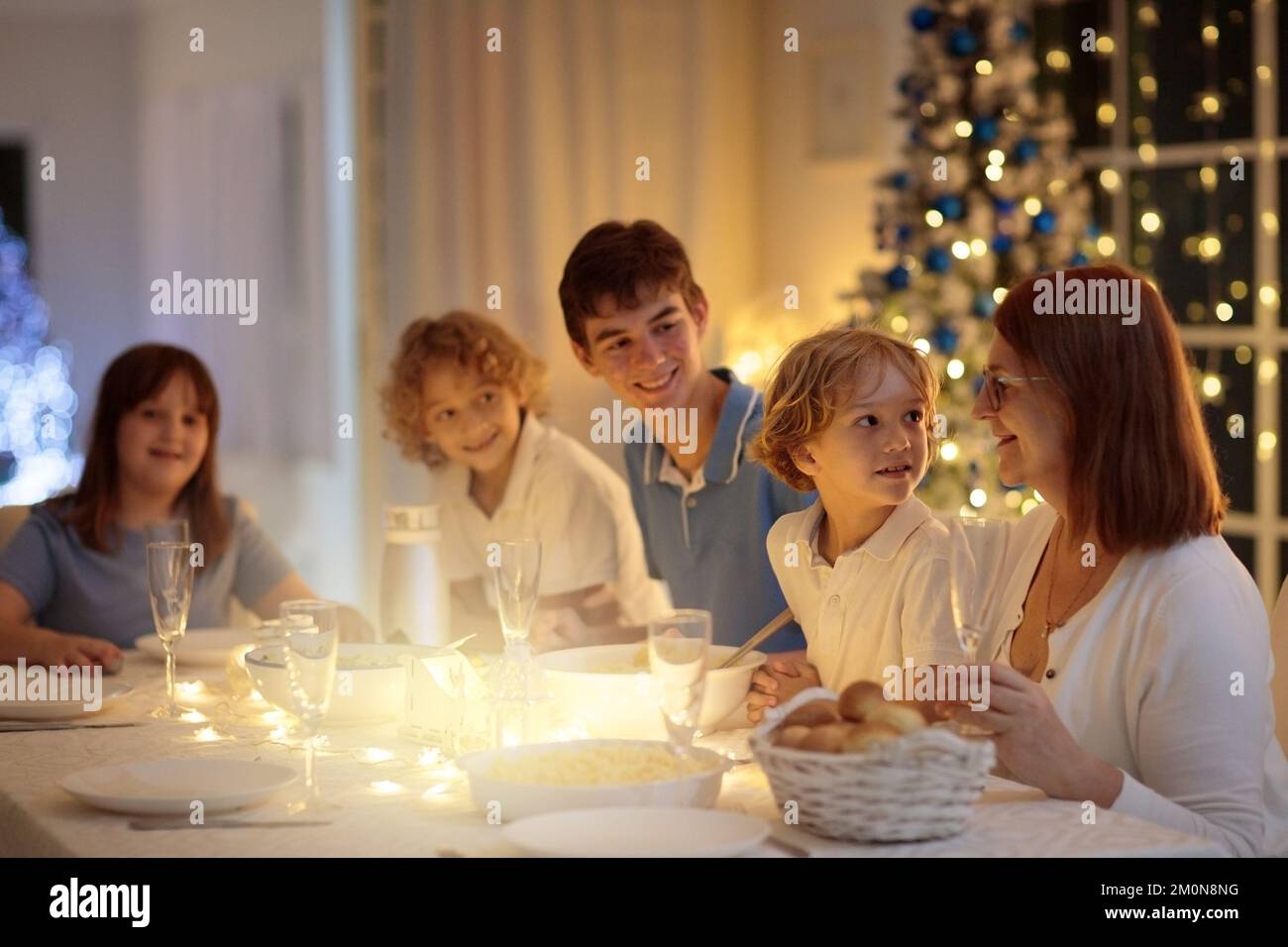 Family with children eating Christmas dinner at fireplace and decorated ...