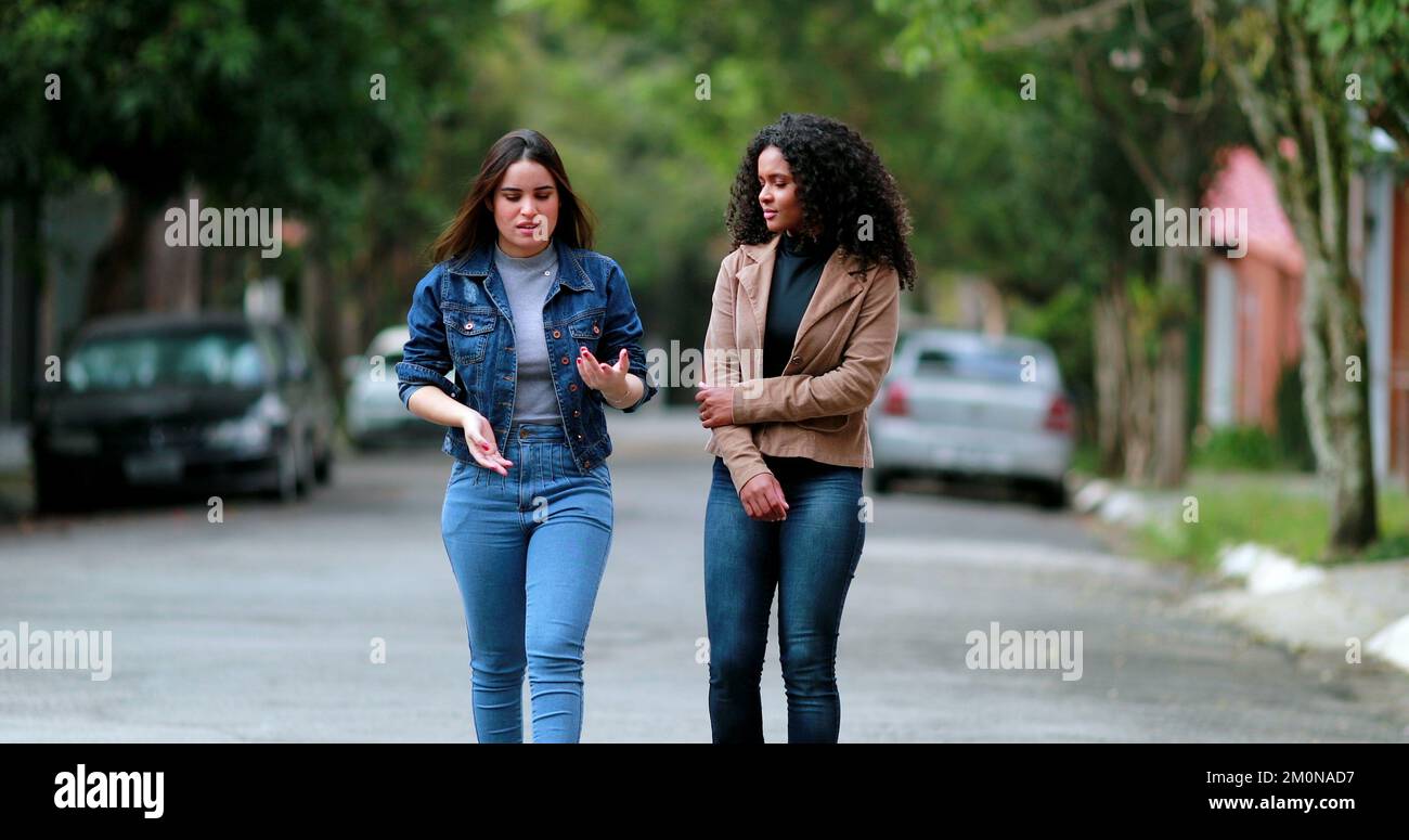 Two women walking together in conversation. Diverse girlfriends ...