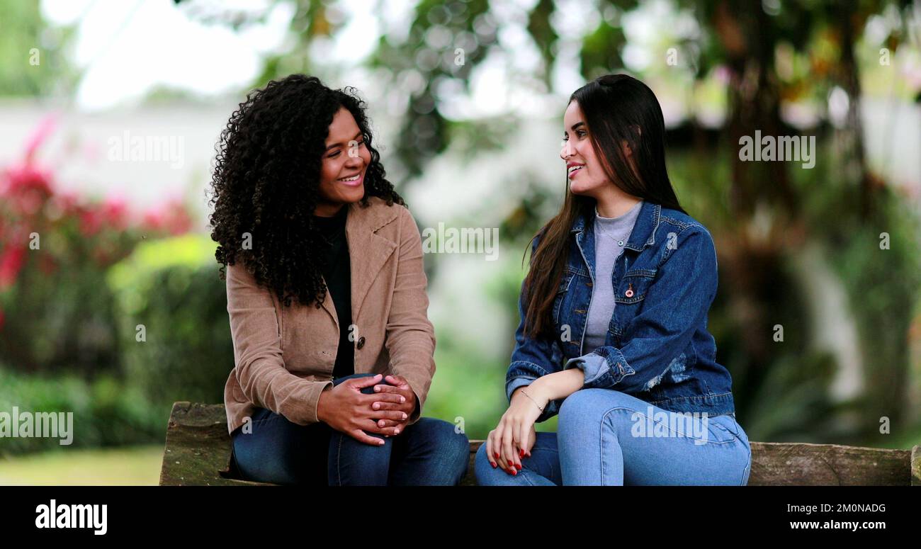 Two young women talking in conversation outside at park Stock Photo - Alamy