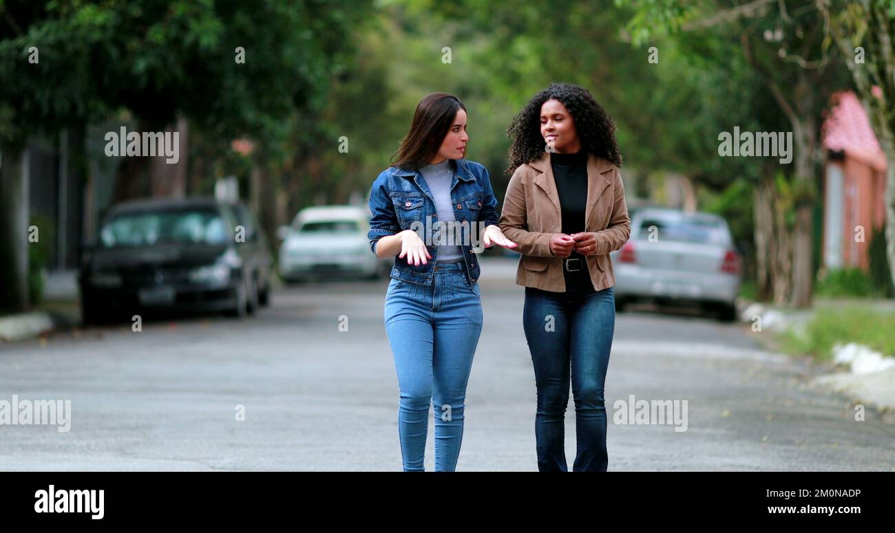 Two women walking together in conversation. Diverse girlfriends ...
