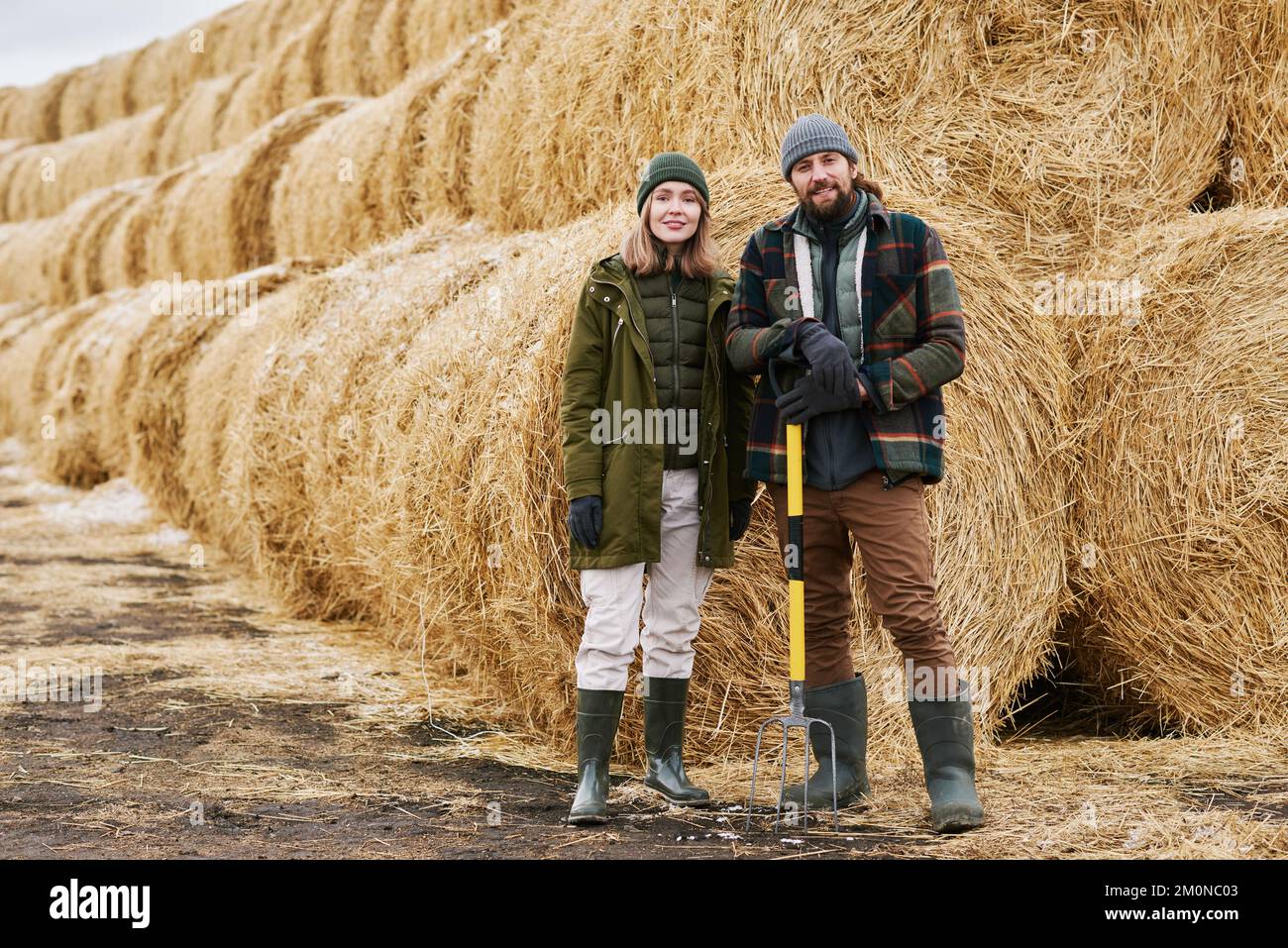 Portrait of young couple of farmers standing outdoors against stack of ...
