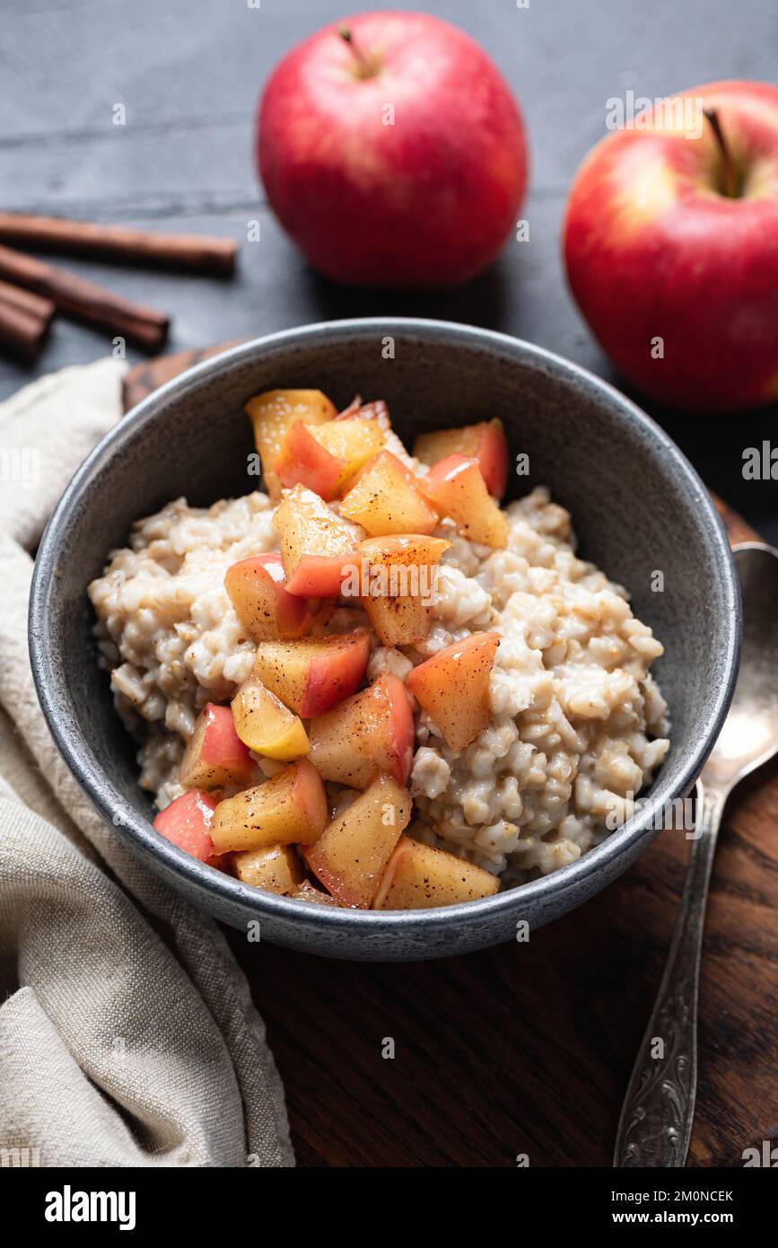 Caramelized apple cinnamon oatmeal porridge bowl on wooden serving board, closeup view, healthy ...