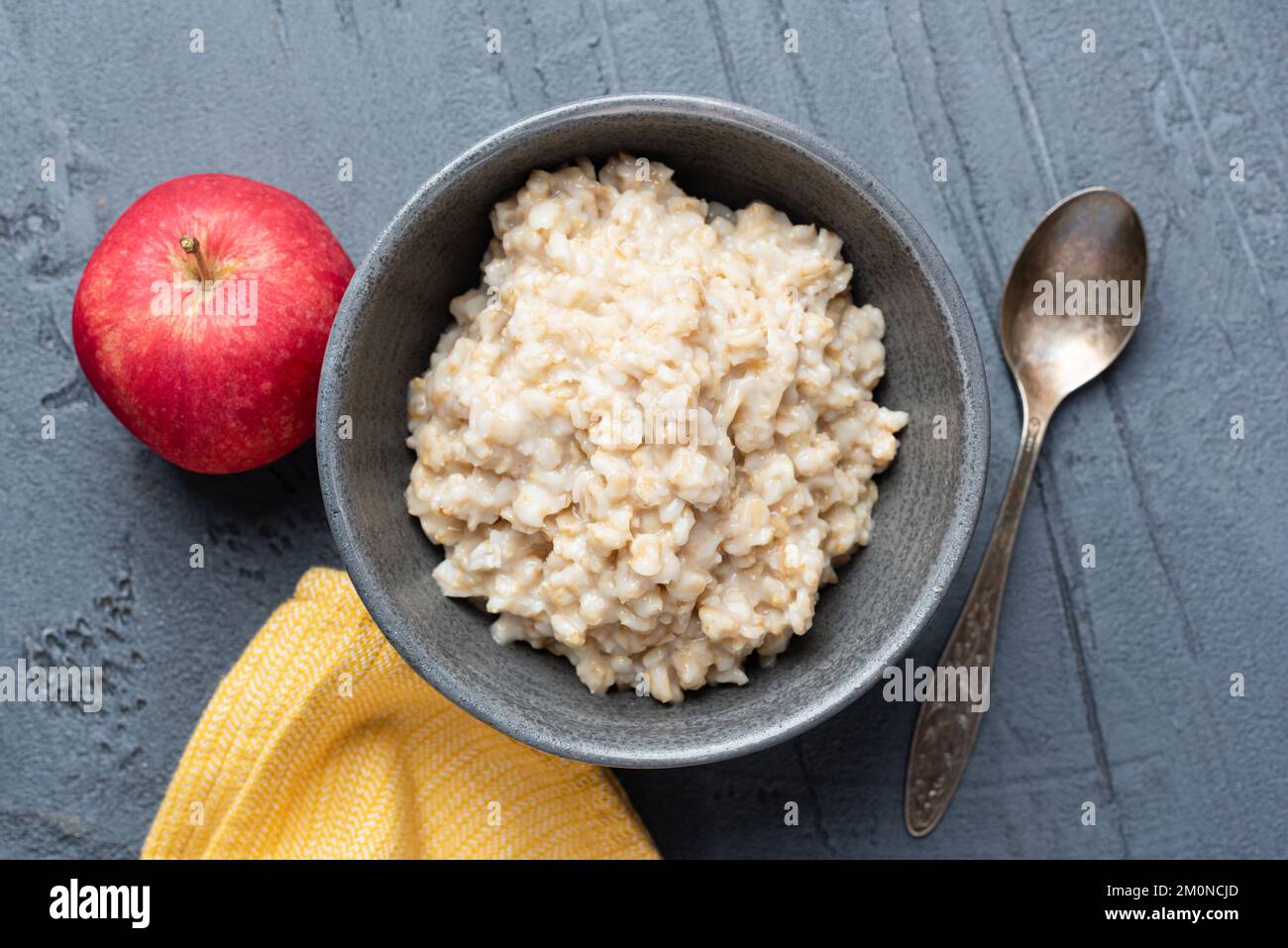 Rolled oats, cooked oatmeal porridge in bowl served with red apple ...