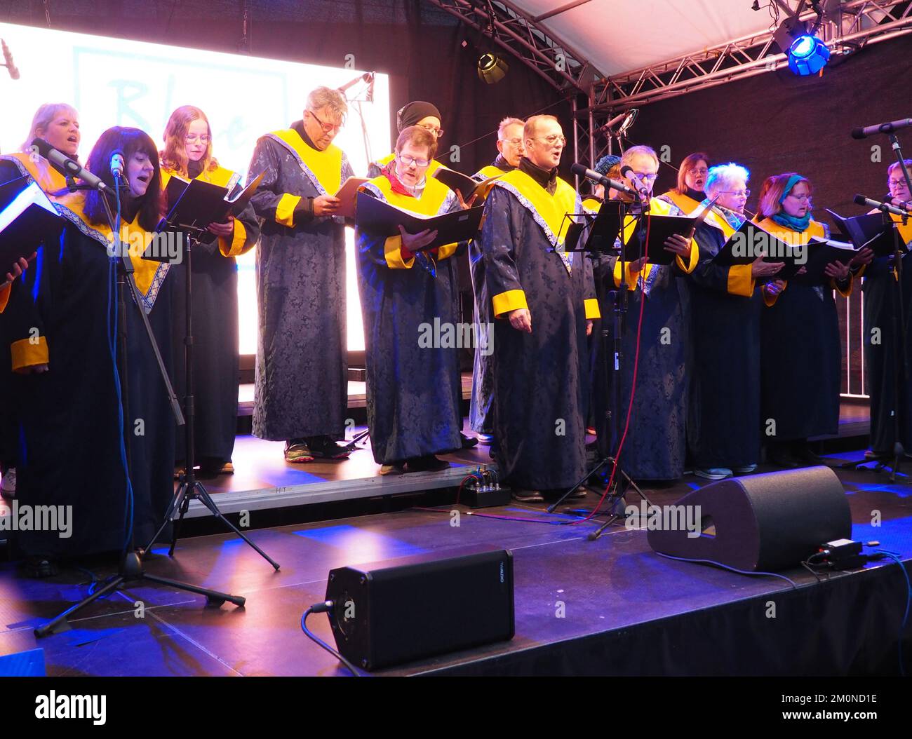 A mixed gospel choir singing with notebooks on an outdoor stage ...