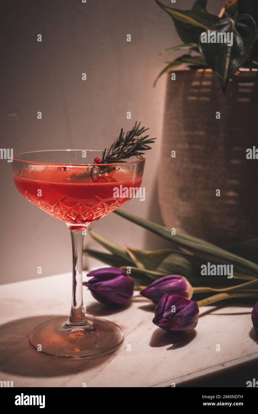 A closeup of a red cocktail with a beautiful garnish next to the purple ...