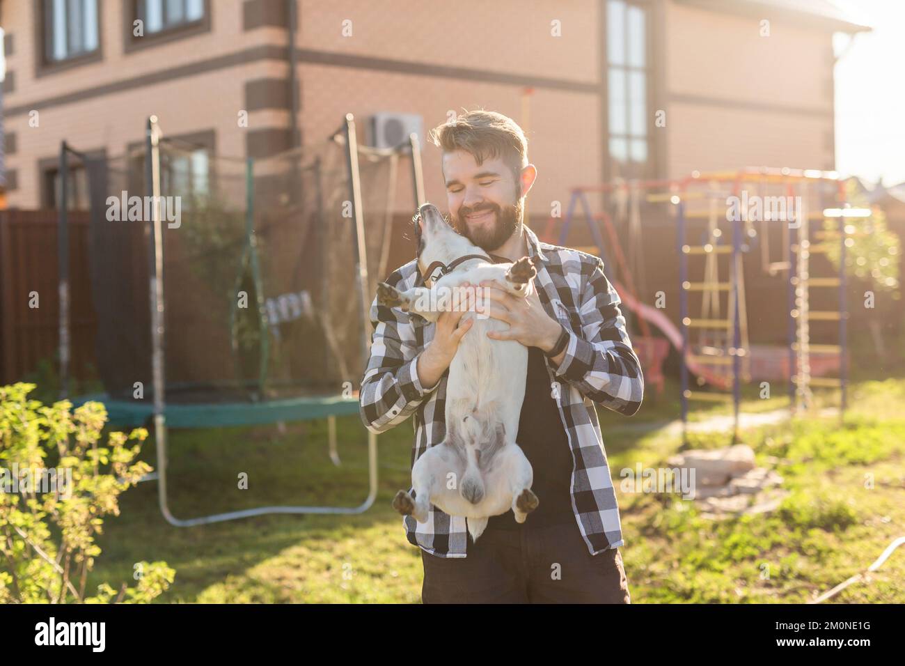 Young man holding jack russell terrier dog near his house on backyard ...