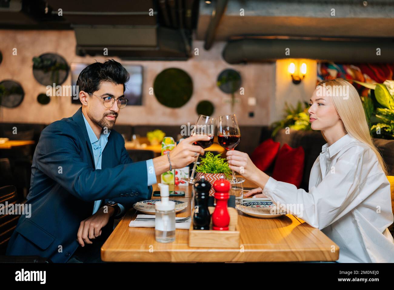 Side view of elegant young couple in love clinking glasses of red wine ...