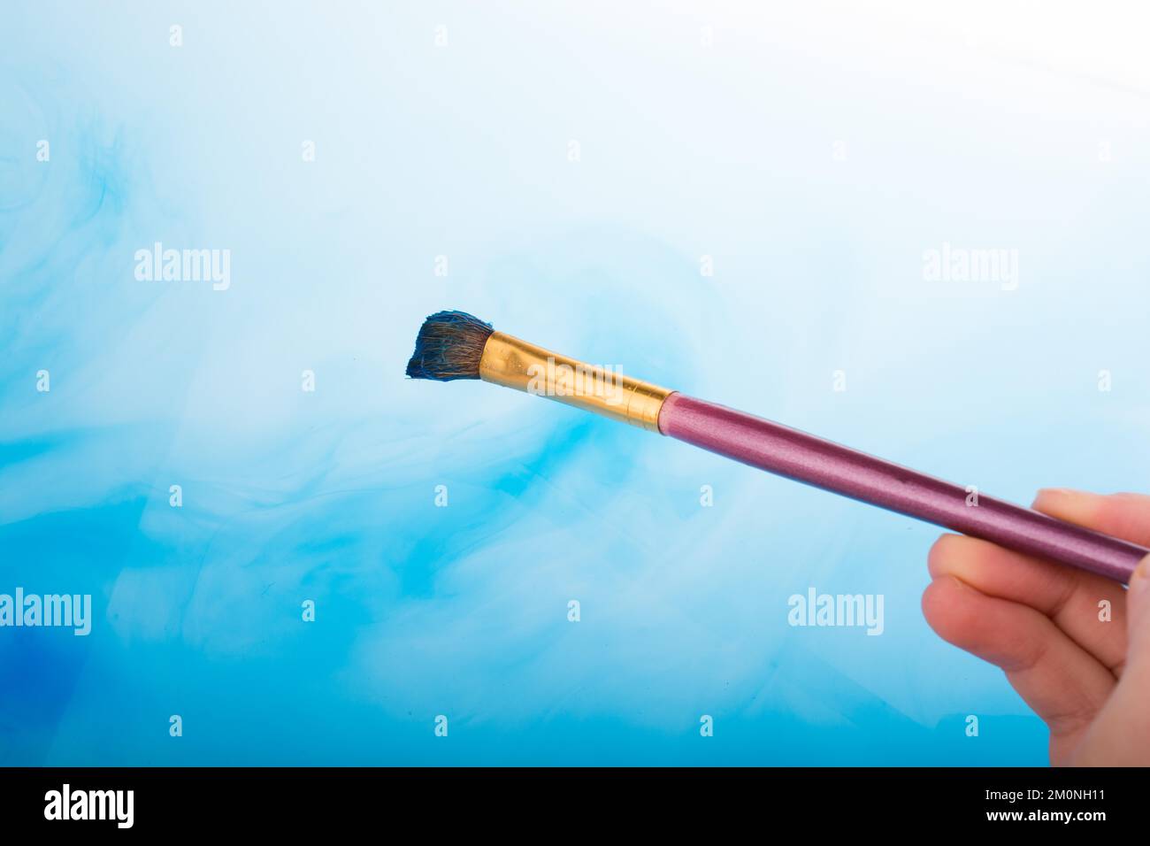 Watercolor paint dissolving in water as painting brush touches water ...