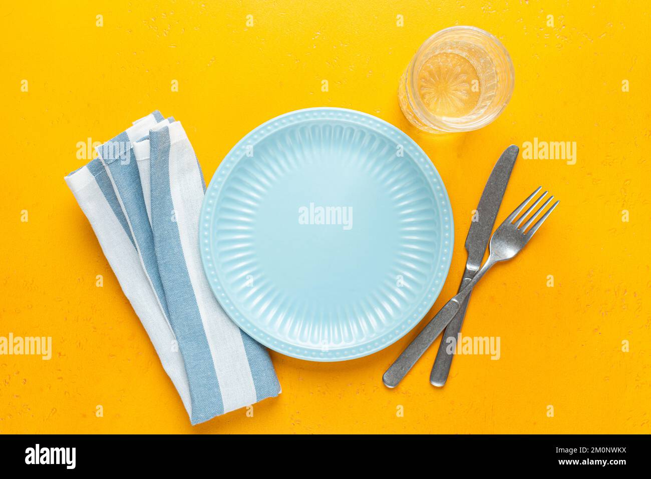 Empty blue plate, table textile and cutlery on yellow background. Table ...