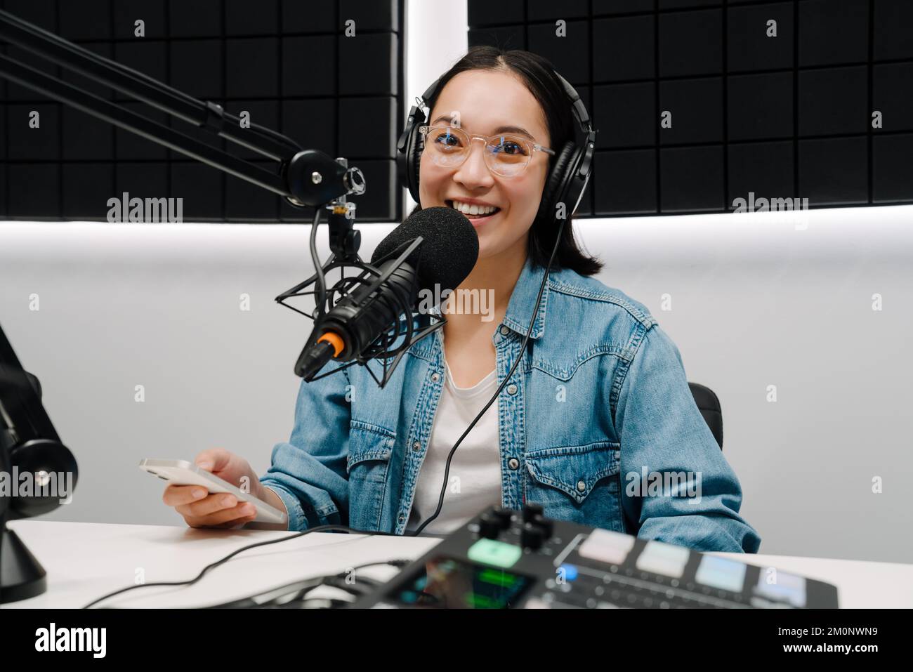 Beautiful happy young female radio host using microphone and headphones ...