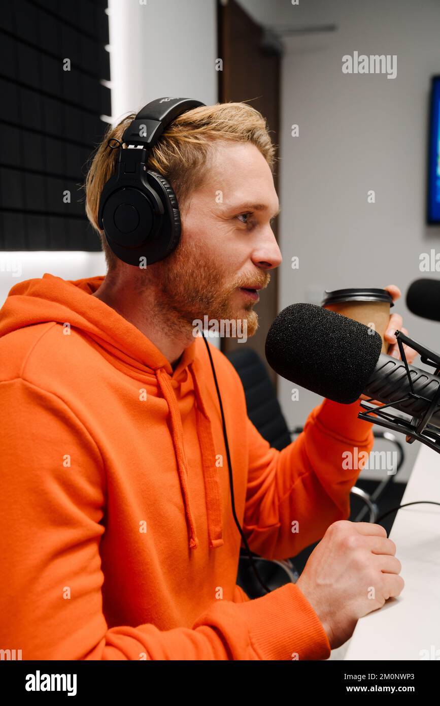 Happy young male radio host using microphone and headphones while ...