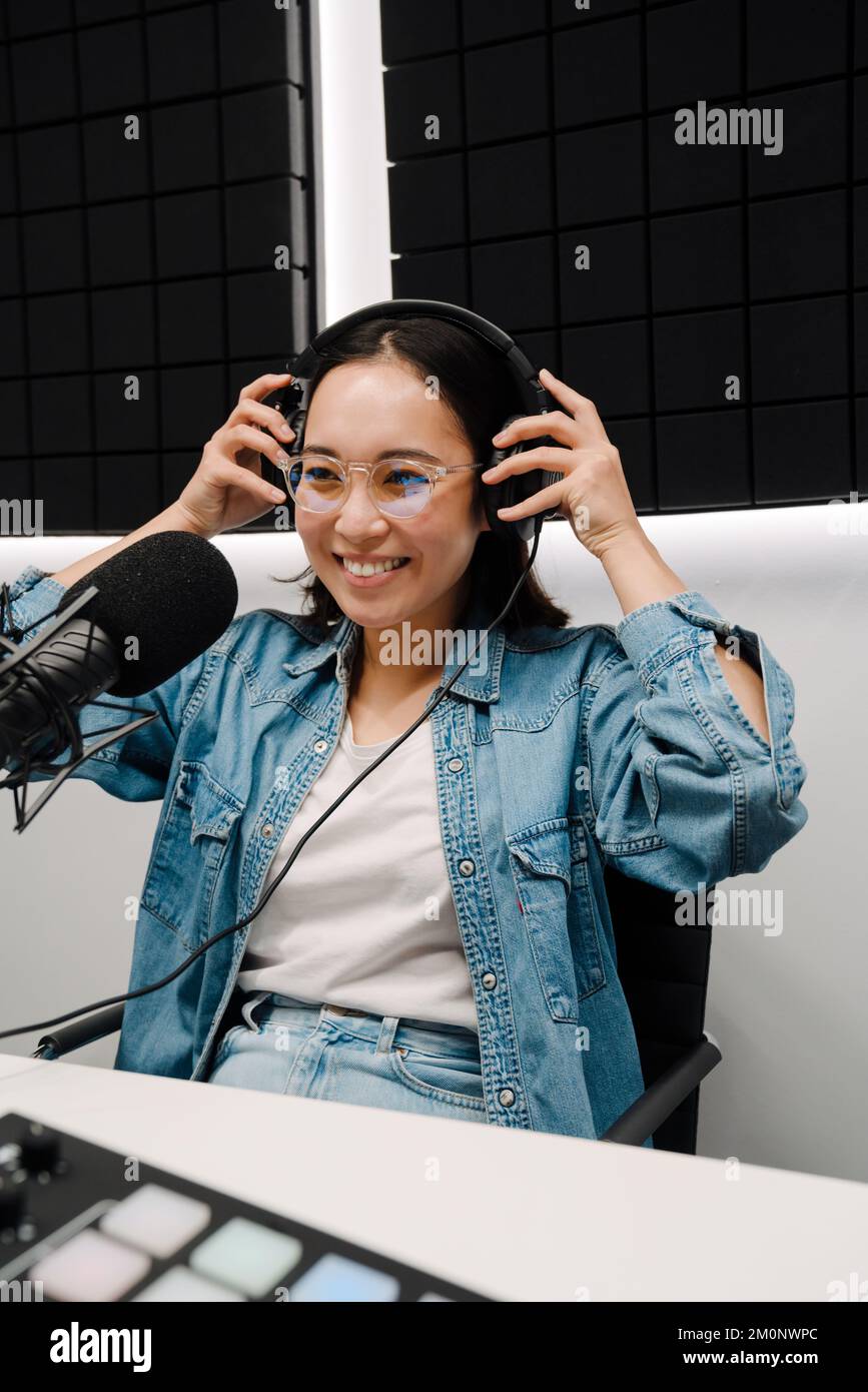 Beautiful happy young female radio host using microphone and headphones ...