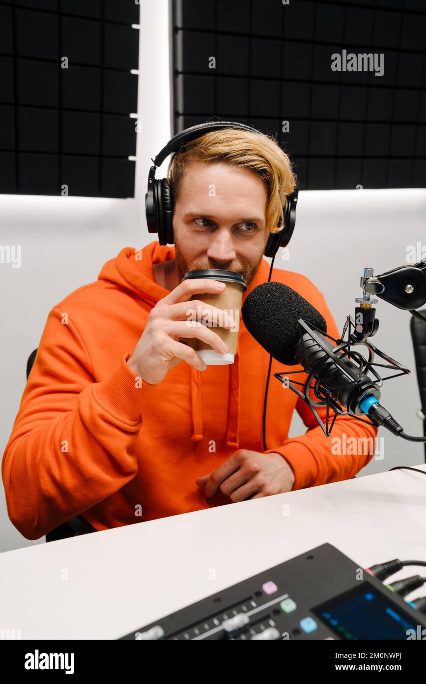 Happy young male radio host using microphone and headphones while ...