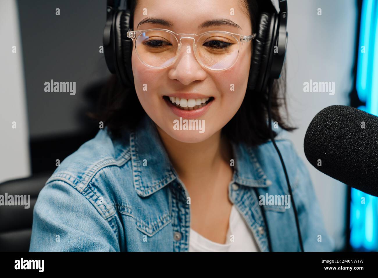 Beautiful happy young female radio host using microphone and headphones ...