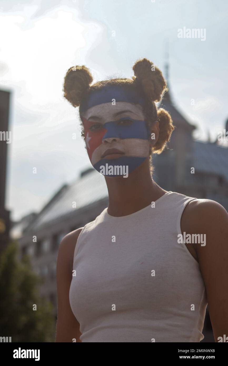 A vertical shot of a young female with the Cuban flag painted on her ...