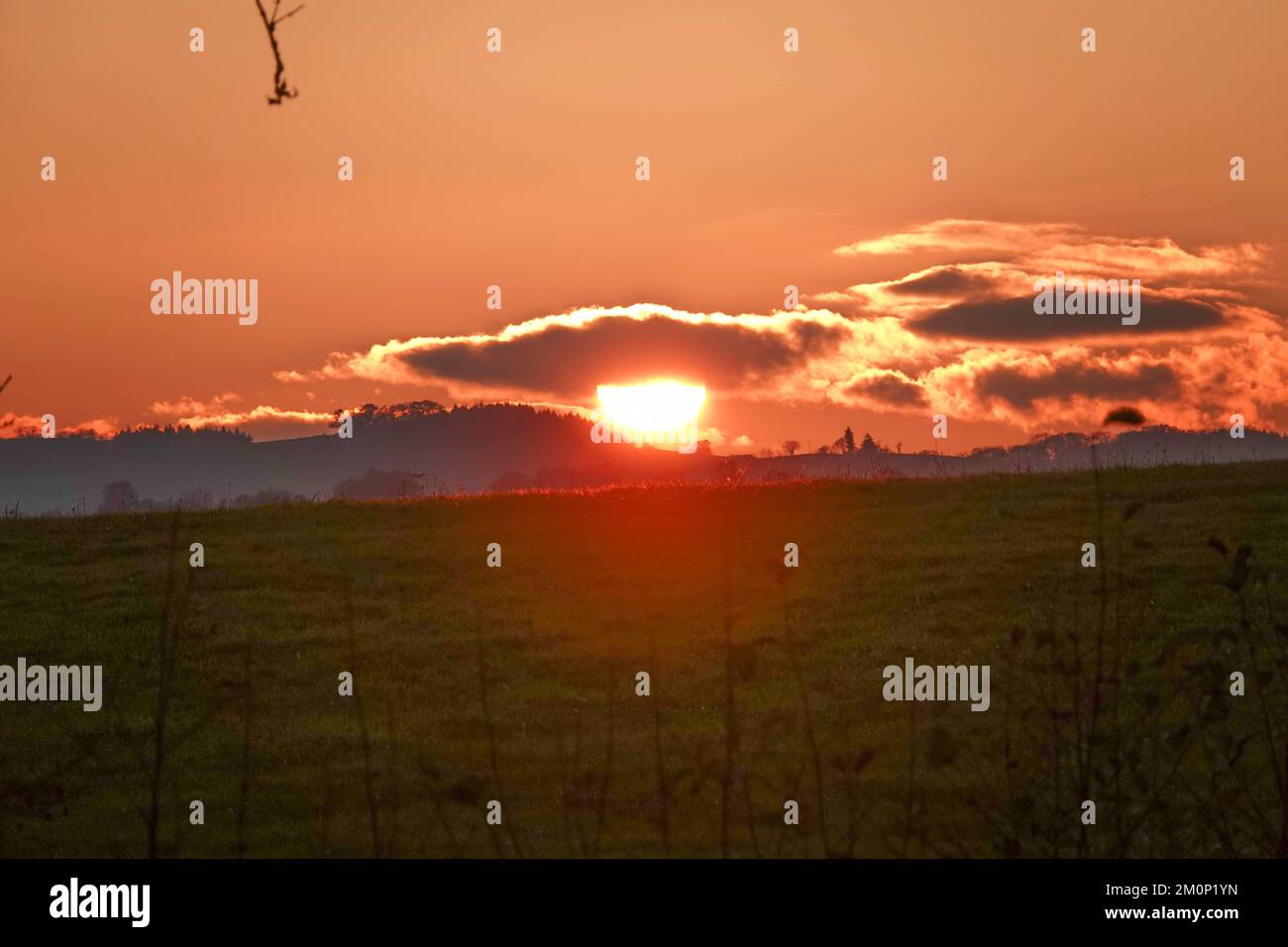 A sunset view over the field red sun setting behind clouds making sky ...