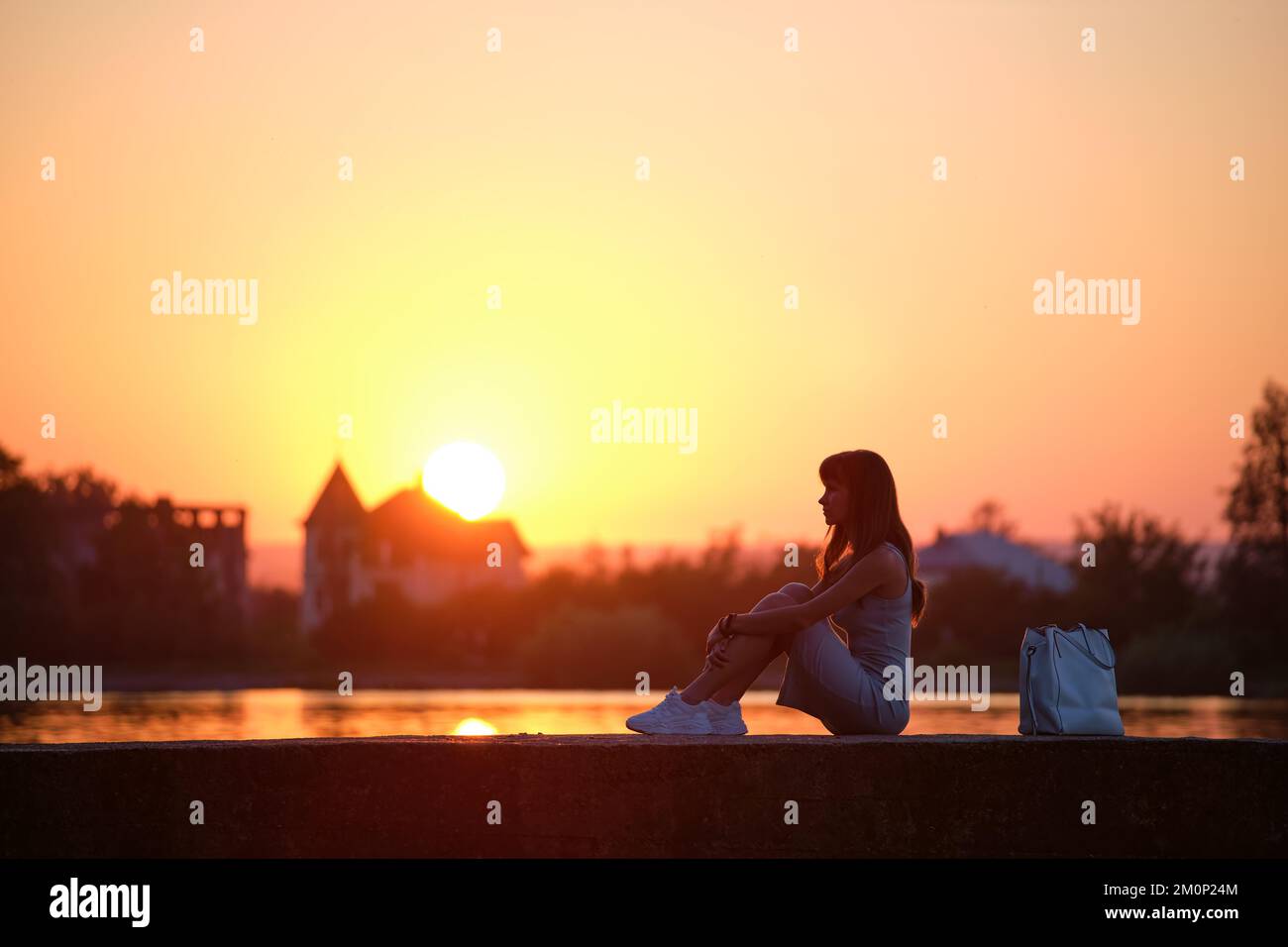 Lonely woman sitting alone on lake shore on warm evening. Solitude and ...