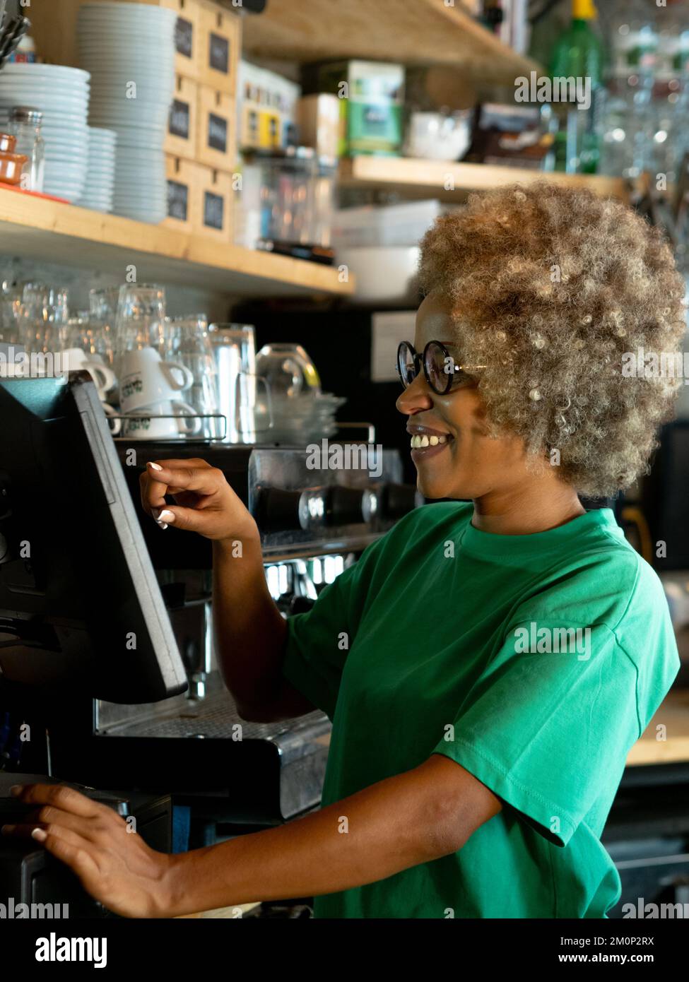 Happy African American female waitress using cash register while ...