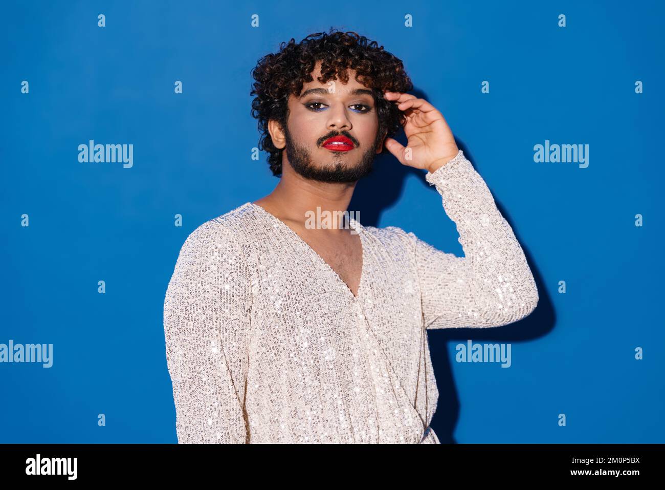 Young curly man with makeup posing and looking at camera isolated over ...