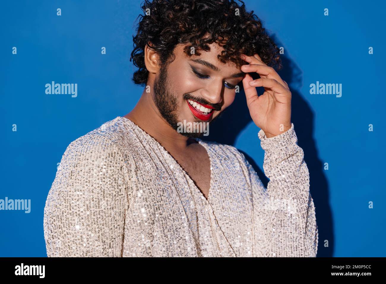 Young curly man with makeup posing and smiling at camera isolated over ...