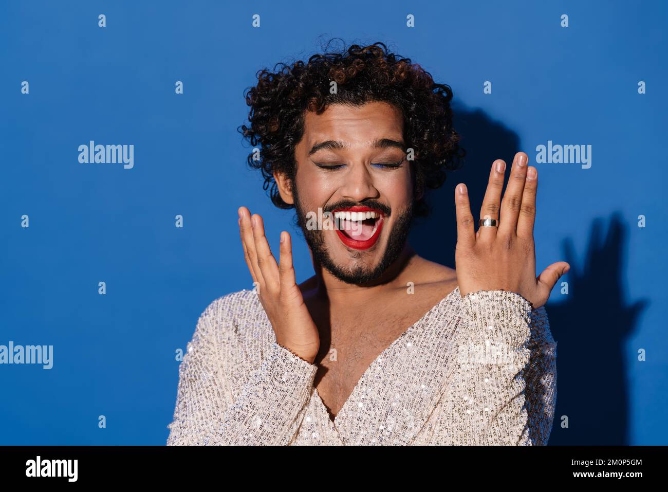 Young excited man with makeup laughing at camera isolated over blue ...