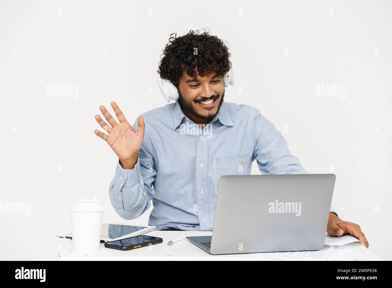 Adult indian smiling curly office employee waving in front of laptop ...