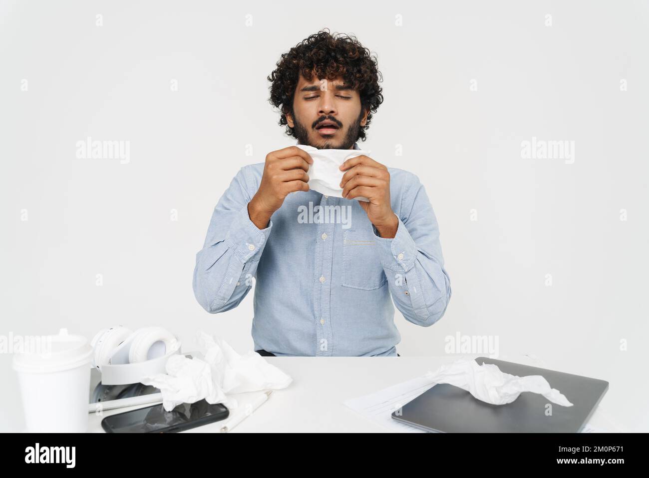 Young indian office employee is sneezing by office table over grey ...